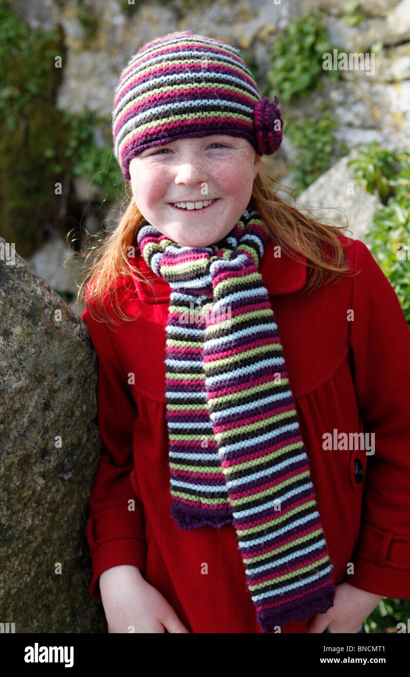 A small girl posing for pictures dressed in red coat and multi colored ...