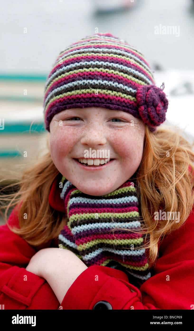 A small girl posing for pictures dressed in red coat and multi colored ...