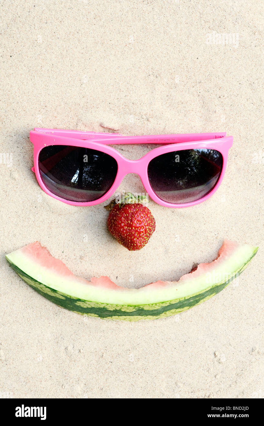 Symbolic happy summer face made out of fruit and sunglasses in the sand ...