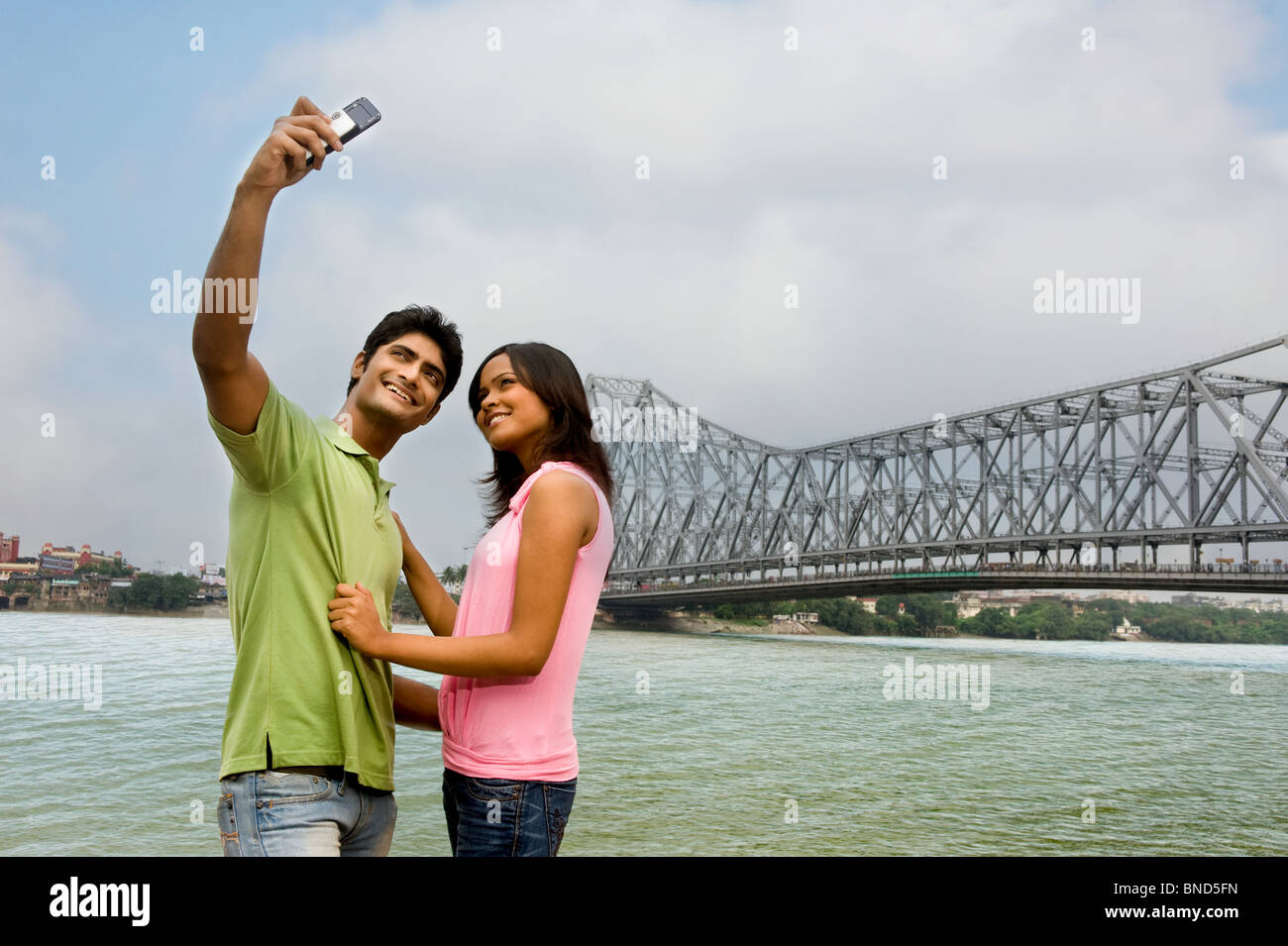 Couple taking a picture of themselves with a bridge in the background ...