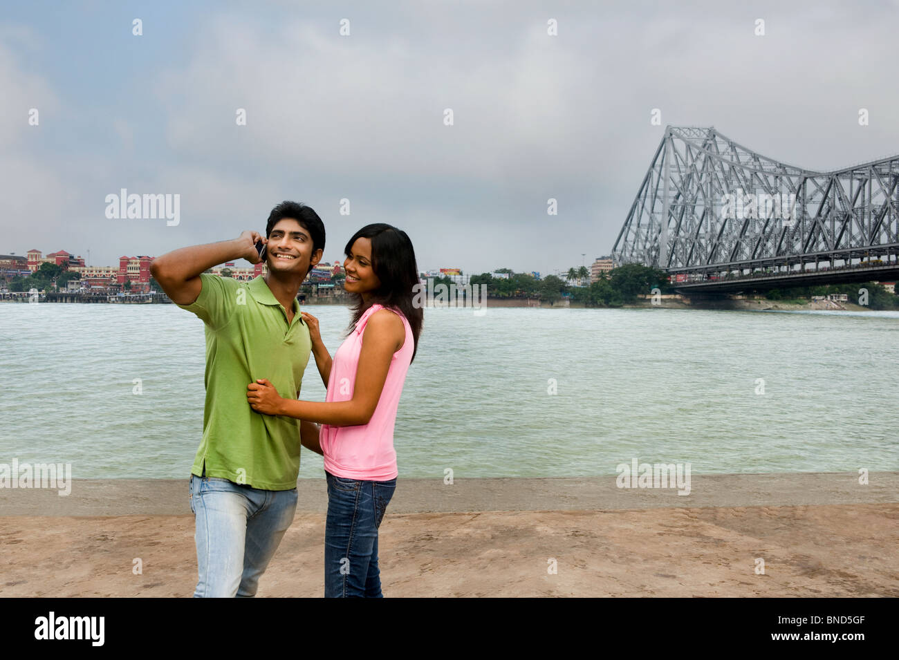 Couple standing together with a bridge in the background, Howrah Bridge ...