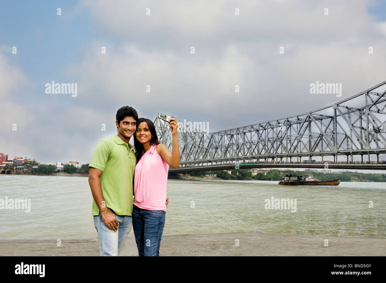 Couple taking a picture of themselves with a bridge in the background ...