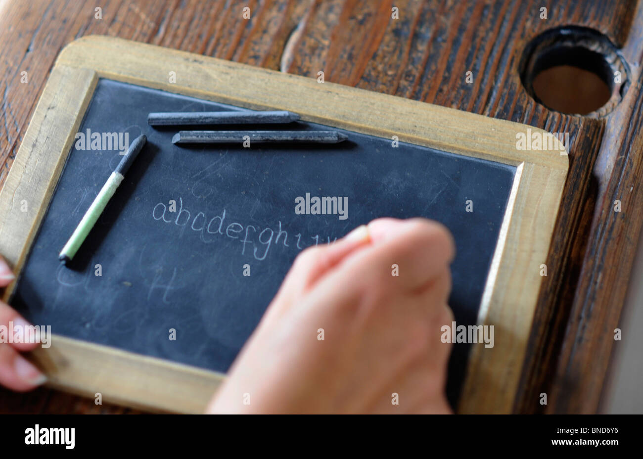 A teacher writes the alphabet in lowercase on a slate with a marker to ...