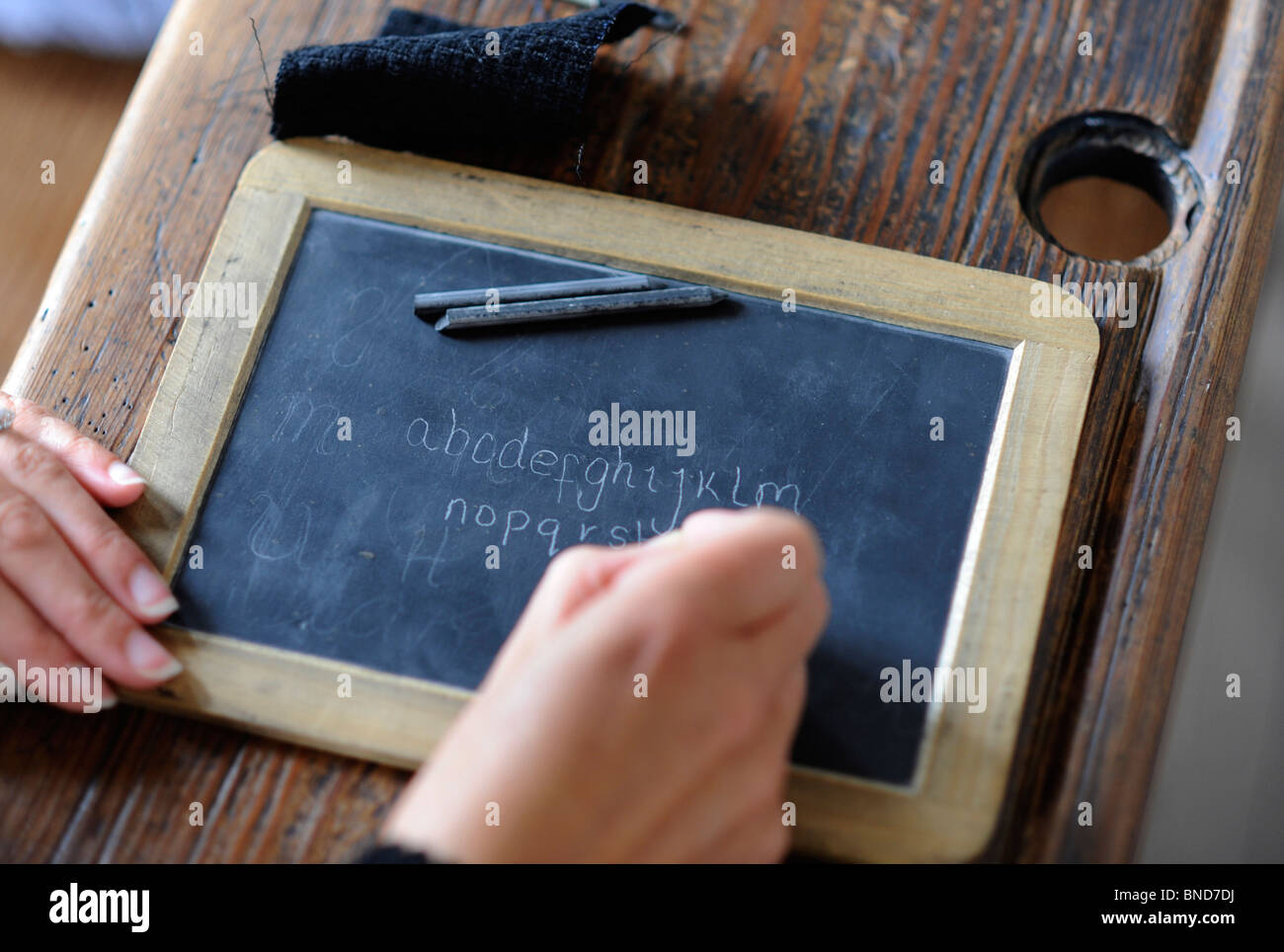 A teacher writes the alphabet in lowercase on a slate with a marker to ...