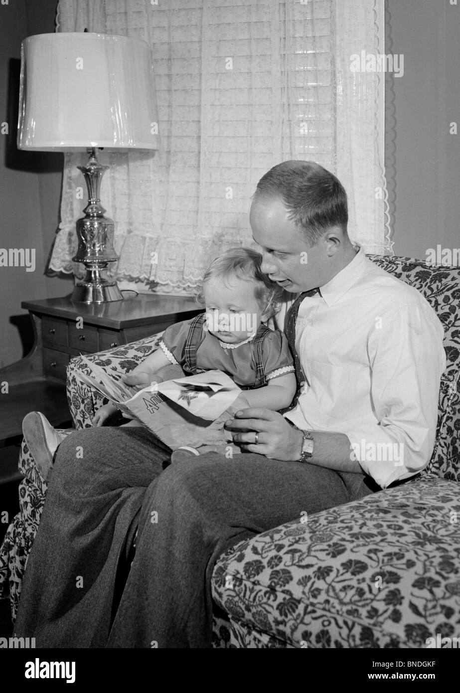 Father reading a book with his daughter sitting on his lap Stock Photo ...
