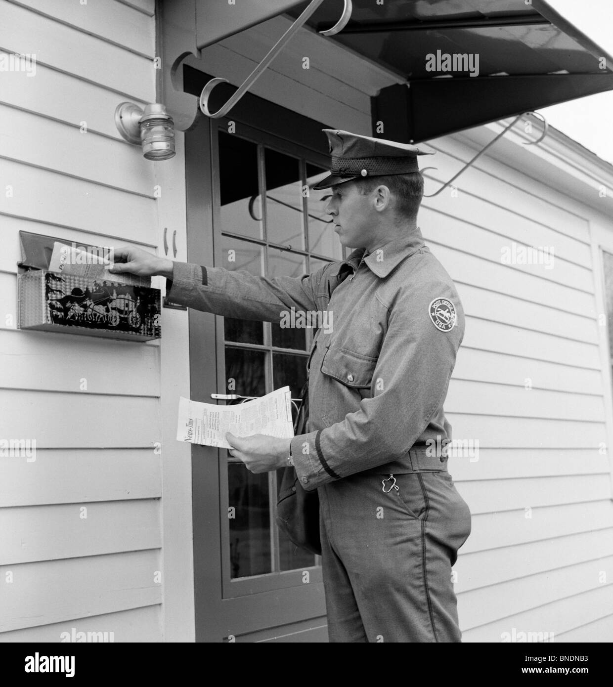 Side profile of a postman dropping mail in a mailbox Stock Photo - Alamy