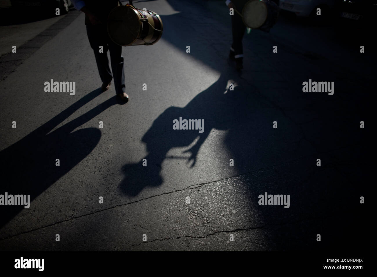 The shadow of men playing a drum and a flute is cast on a road during a ...