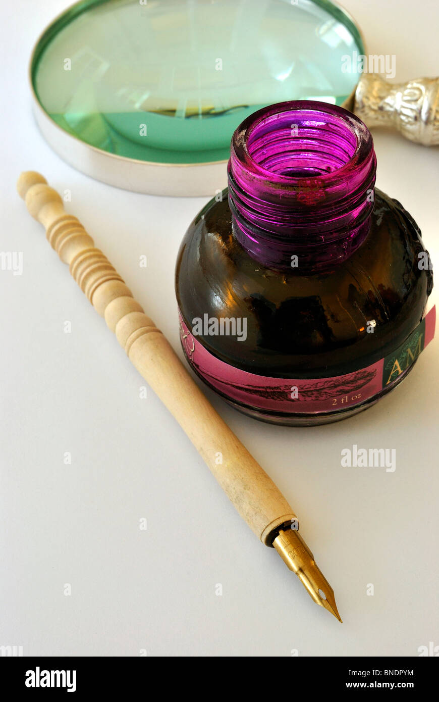 A calligraphy pen, magnifying glass, and inkwell laying on a white ...