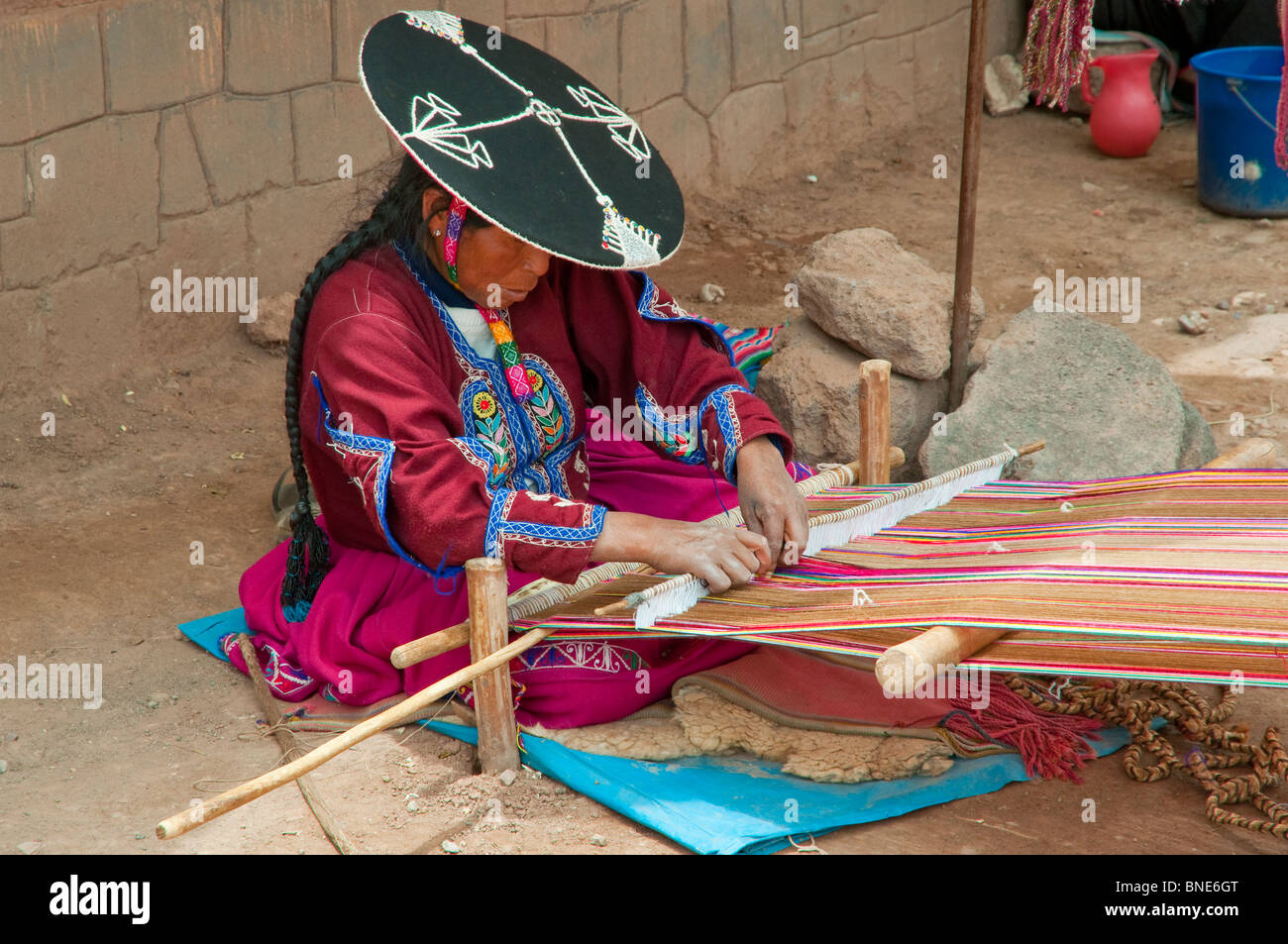 A peruvian woman in traditional dress weaving a blanket in the plaza in ...