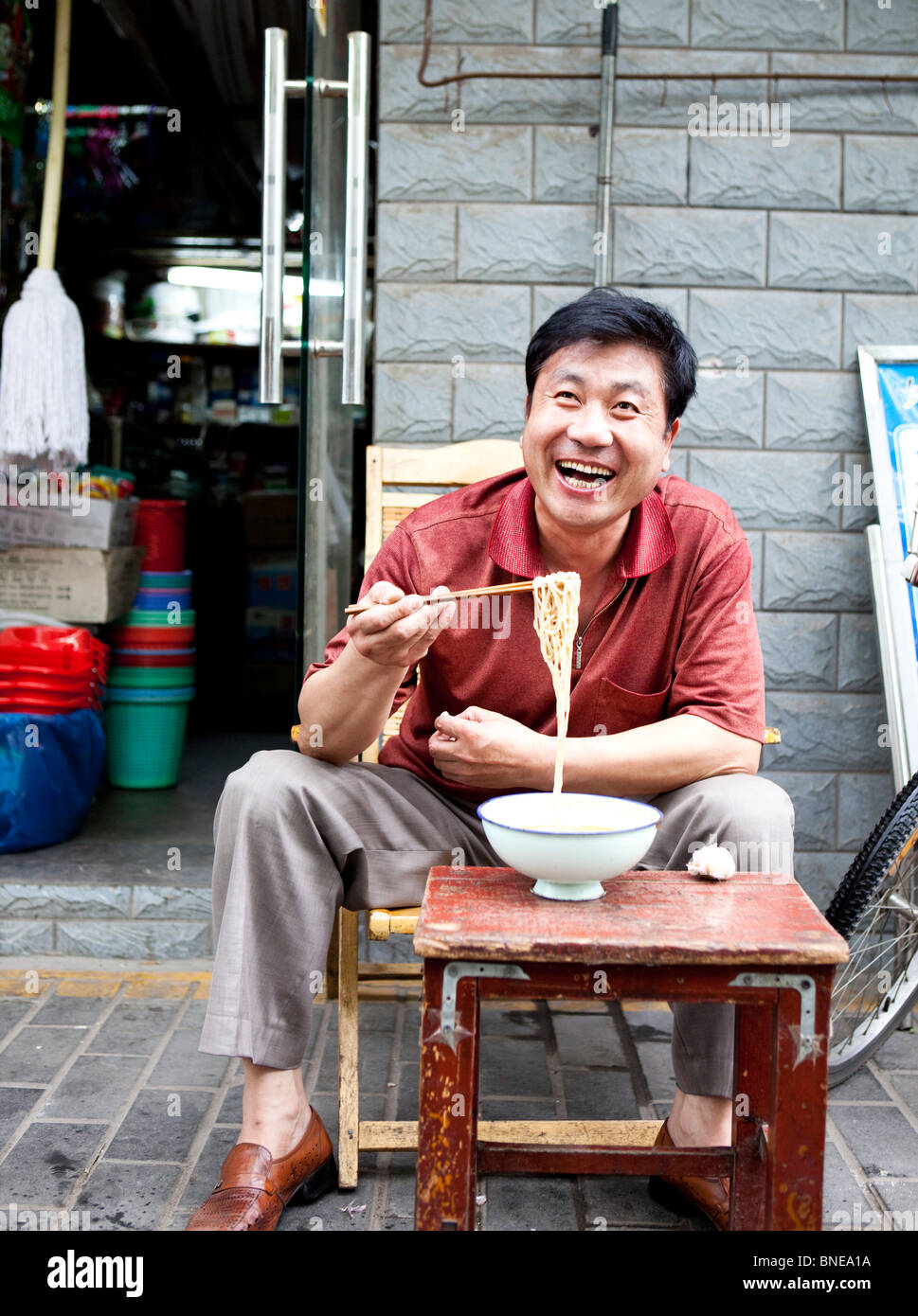 Mature man eating noodles in front of a store, Shanghai, China Stock ...