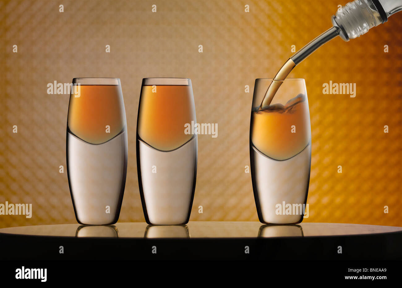 Three shots of liquor two are filled and the third has liquor pouring ...