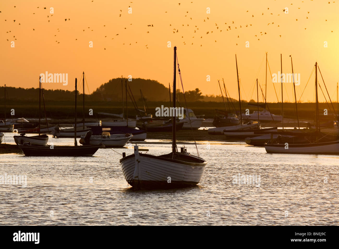The sun setting behind boats moored on the River Burn at Burnham Overy ...