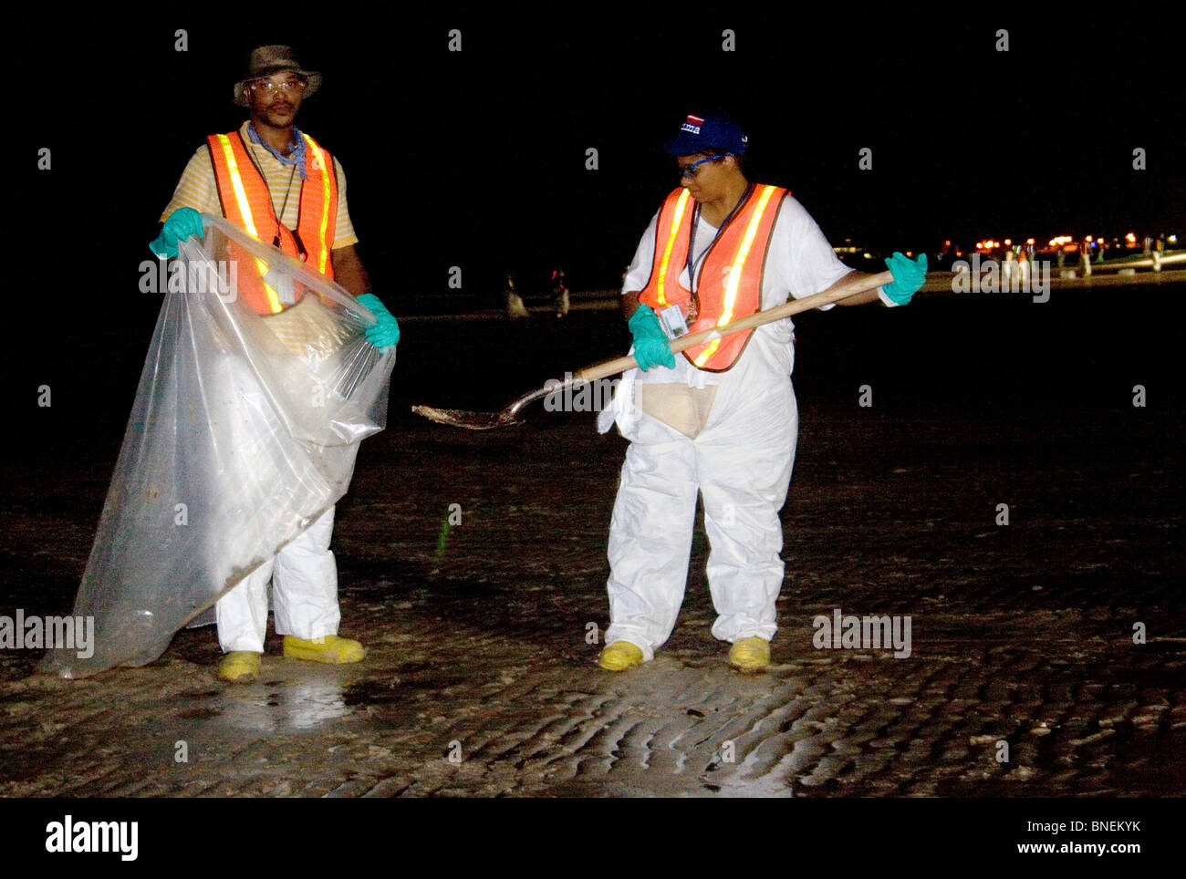 A man and woman bagging up oil & tar at night from a Mississippi beach ...