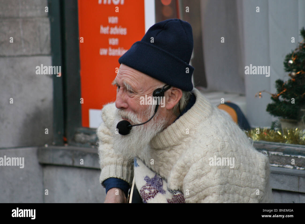 Elderly folk singer with beard, woolly hat and microphone entertains ...