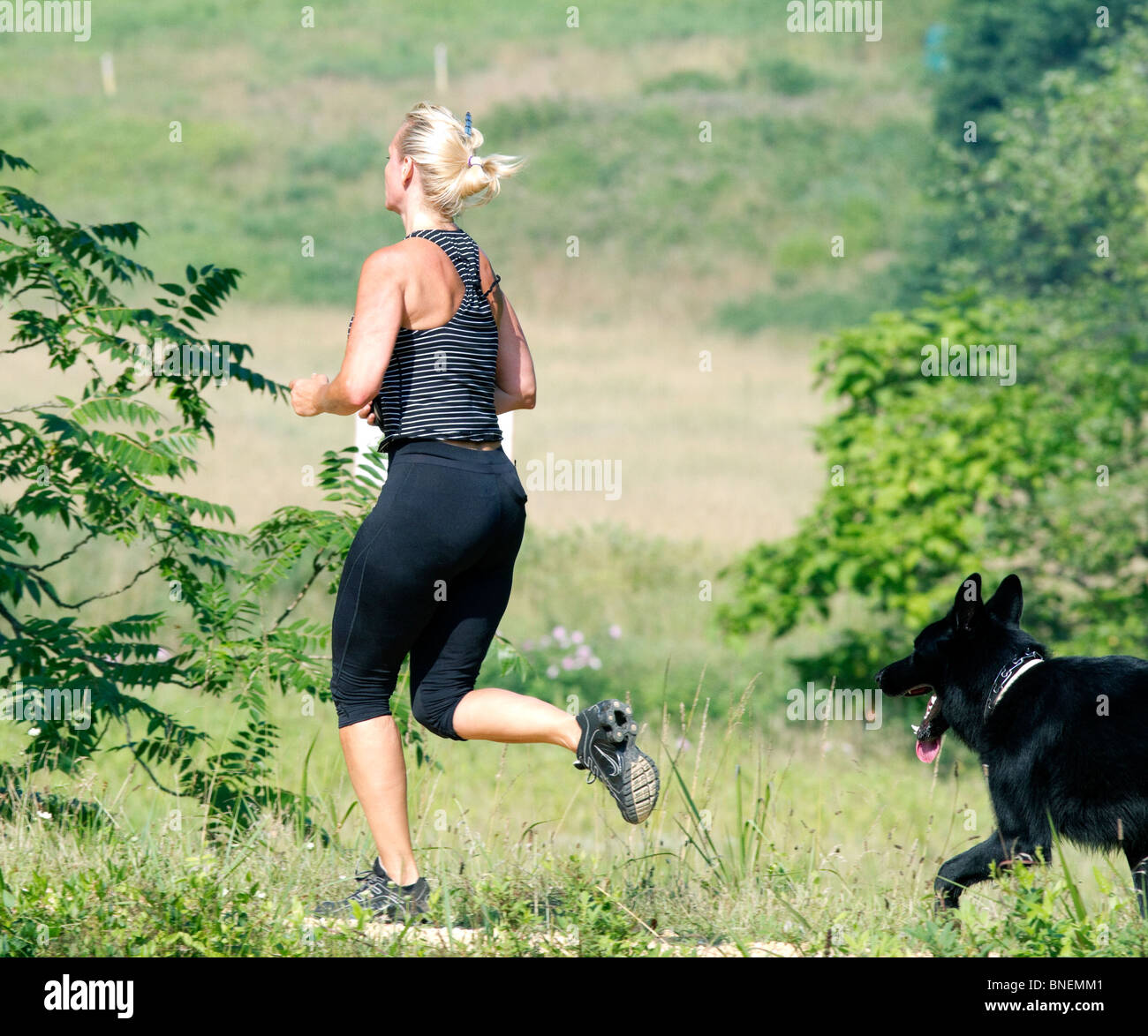 A blond woman female running jogging with her black dog Stock Photo - Alamy