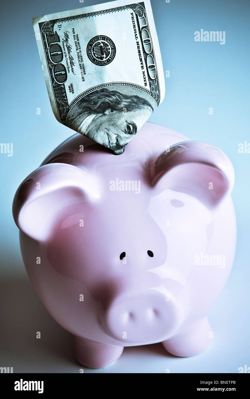 100 dollar bill sticking out of the coin slot of a pink piggy bank ...