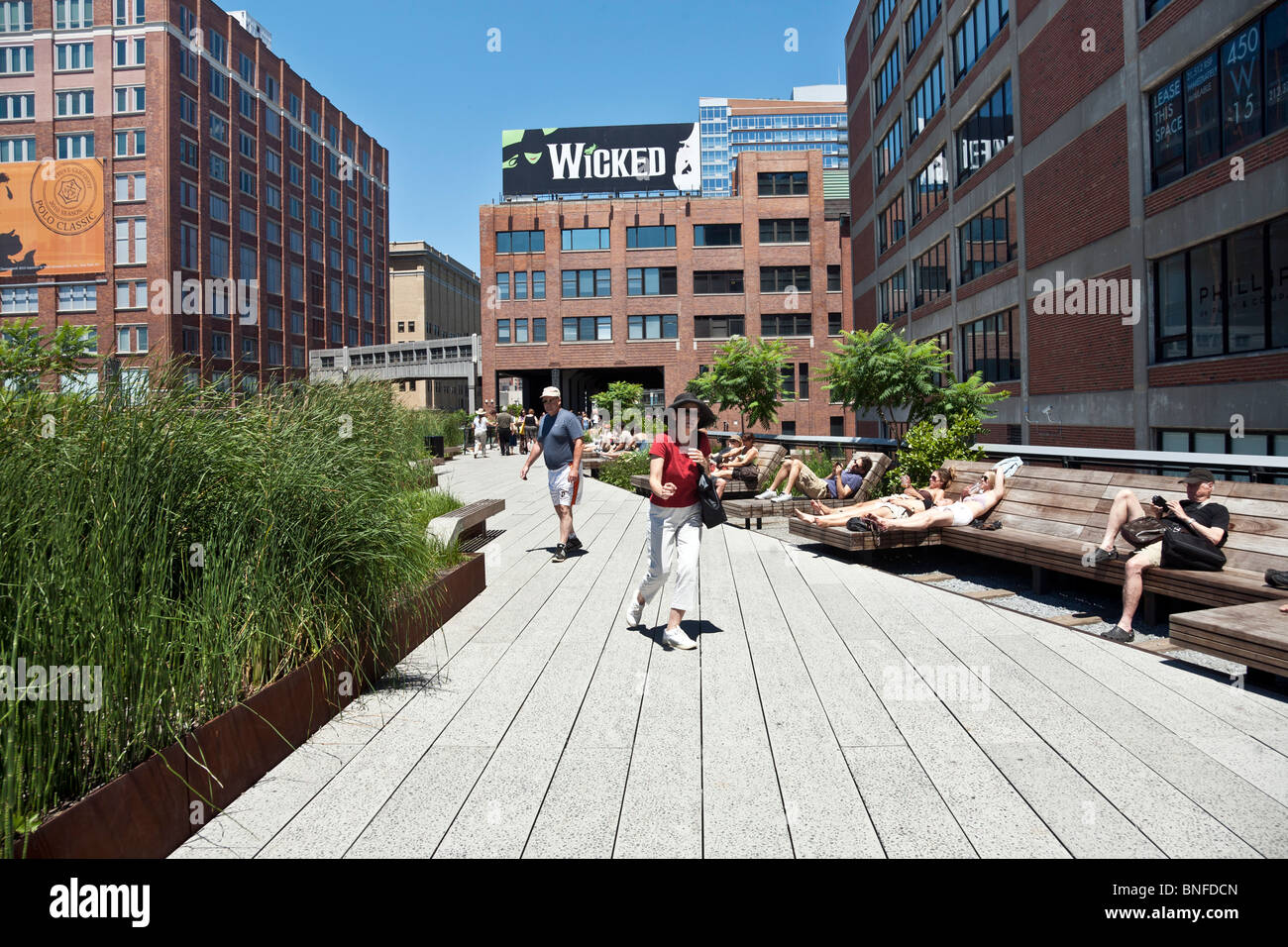 people stroll walkways & bask in sun on wooden recliners & planting ...