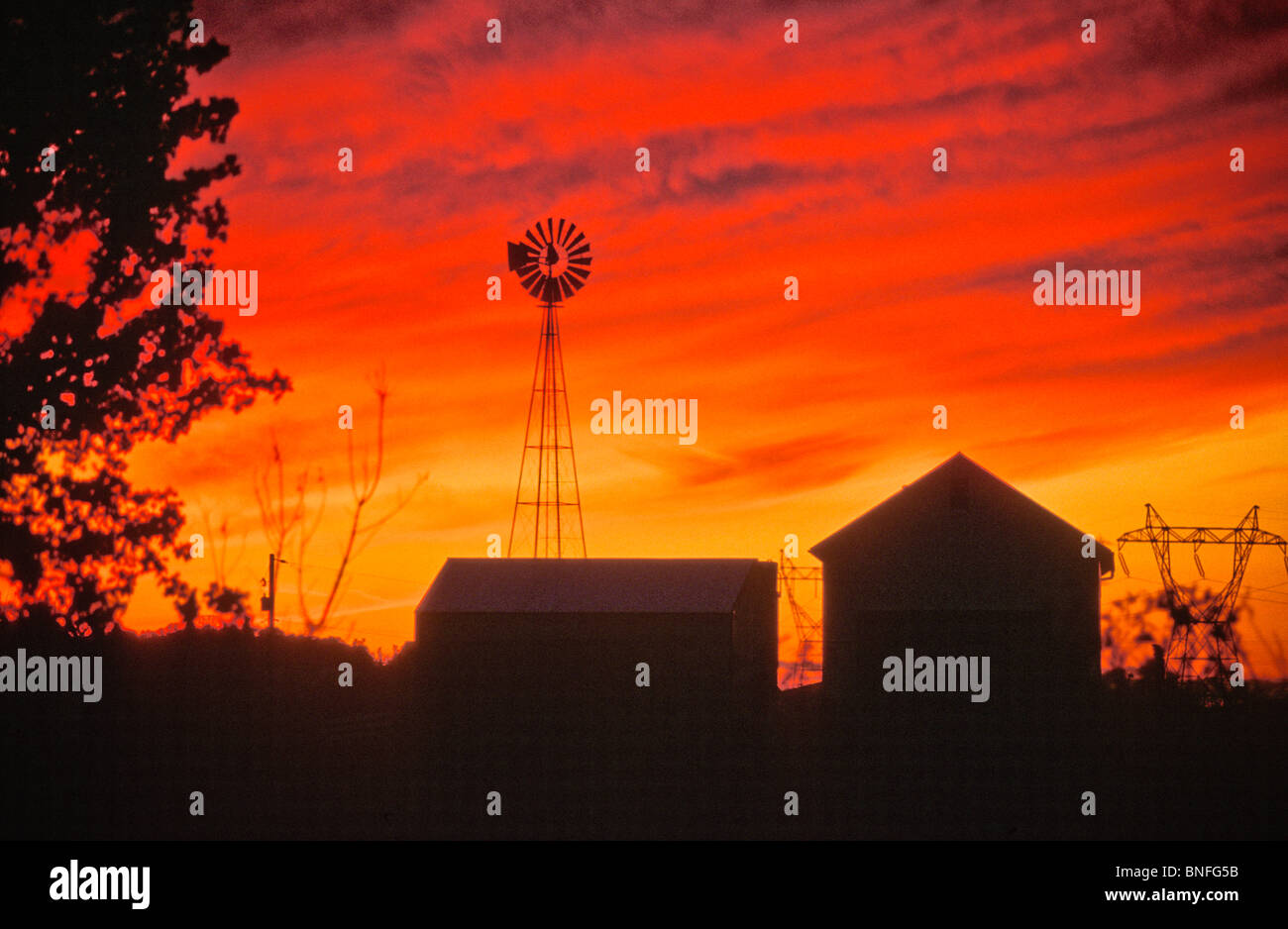 cloudy skies bright red sunset windmill farm buildings barns electric ...