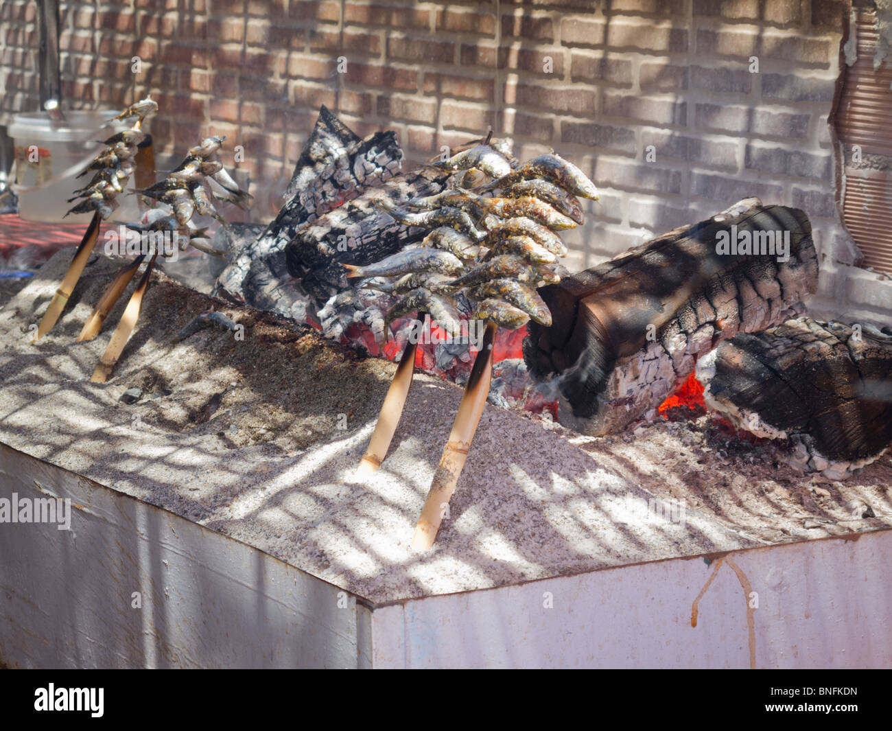 Skewered fish cooking on a wood-fired grill/BBQ in a beach restaurant ...