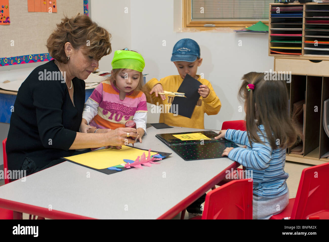 Preschool teacher helping her students with an art project in the ...