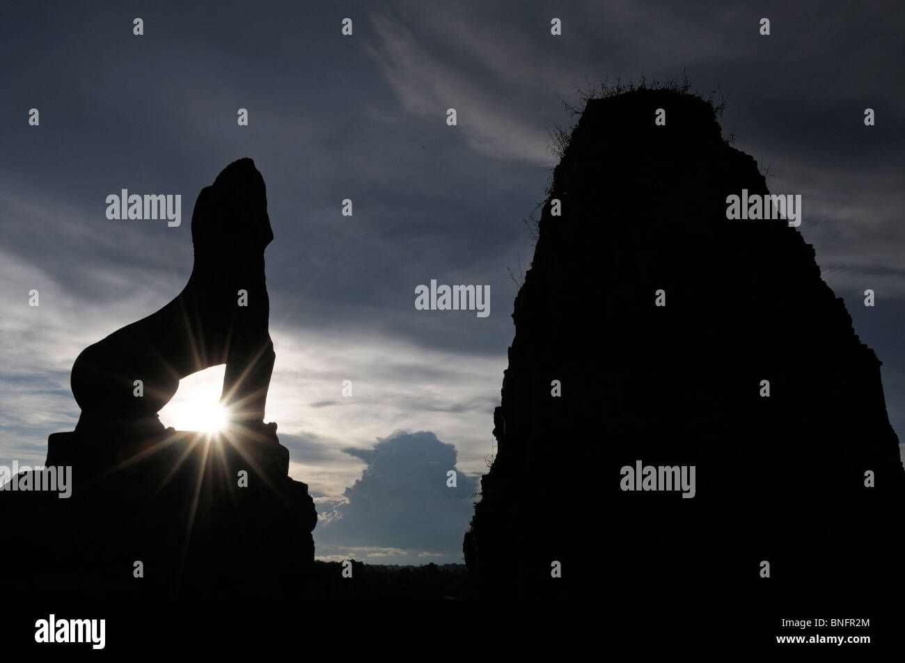 Statue of roaring lion silhouetted against setting sun, Ta Keo Temple ...