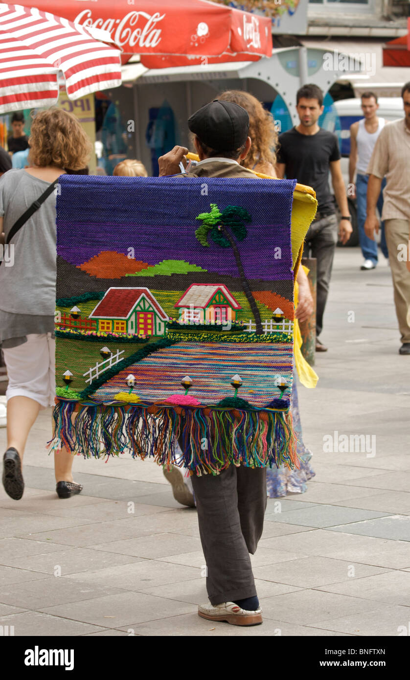 A man carries a selection of brightly coloured woven rugs on his back ...