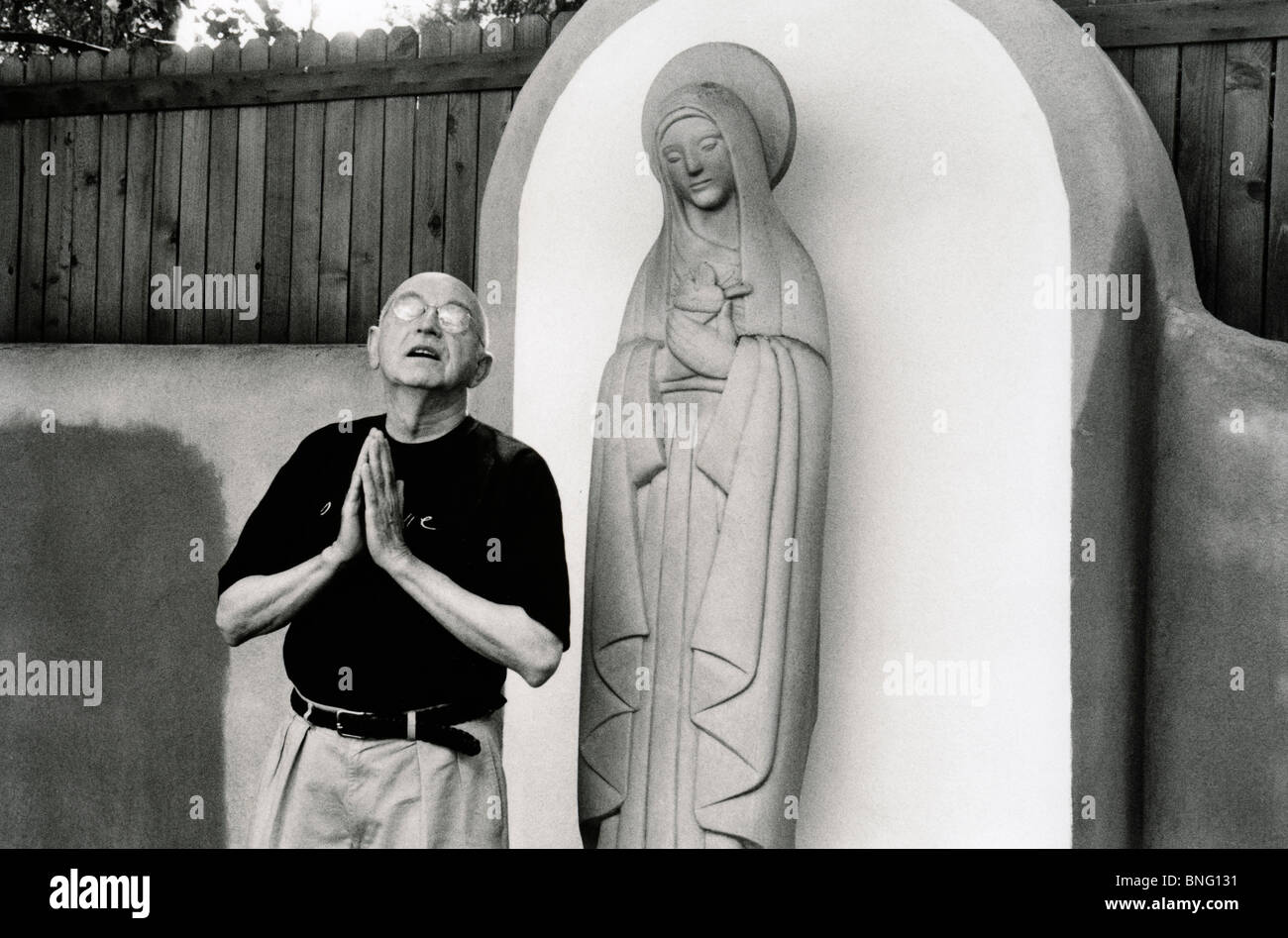 Senior man praying in front of a statue of Virgin Mary, New Mexico, USA ...
