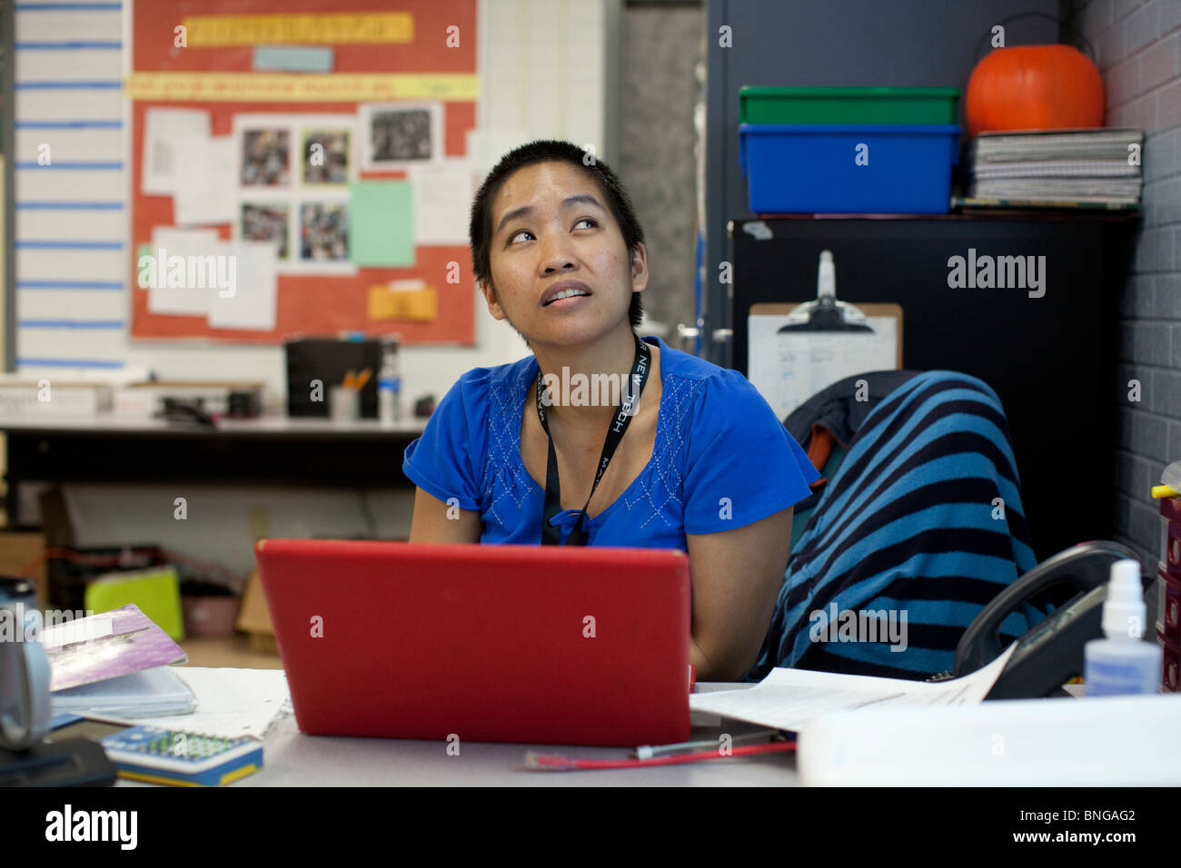 Female physics teacher sits at her desk and listens to a student talk ...
