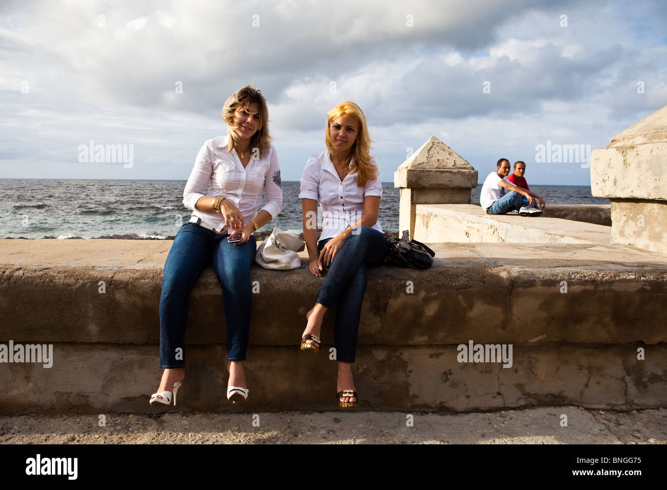 Two girls watched by two boys sit and catch up on the Malecon seafront ...