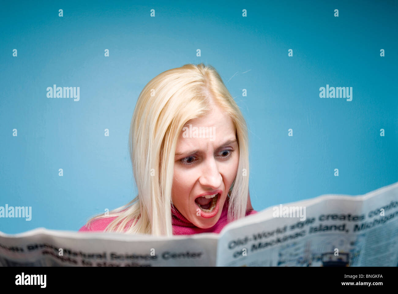 Young woman reading newspaper and looking shocked Stock Photo - Alamy