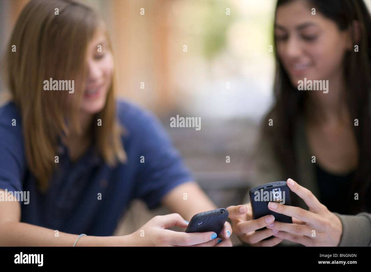 Two female friends text messaging on mobile phones Stock Photo - Alamy