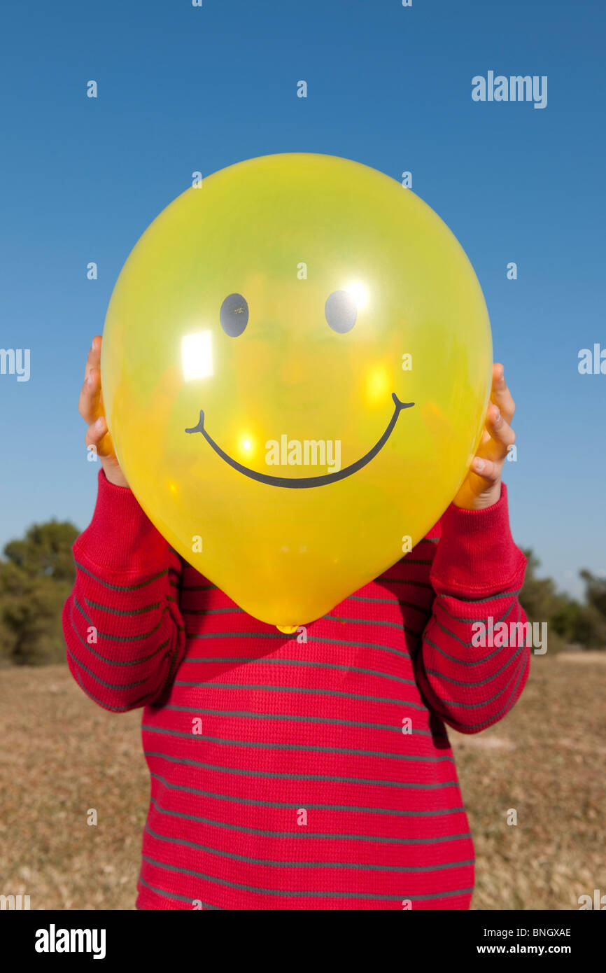 Boy holding a smiley face balloon in front of his face Stock Photo - Alamy
