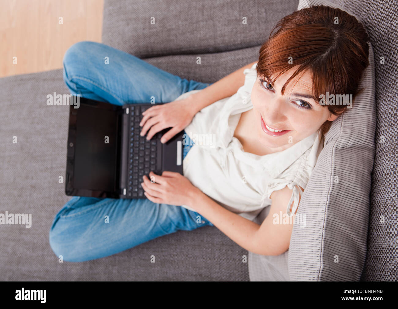 Beautiful woman seated on sofa and working with a laptop Stock Photo ...