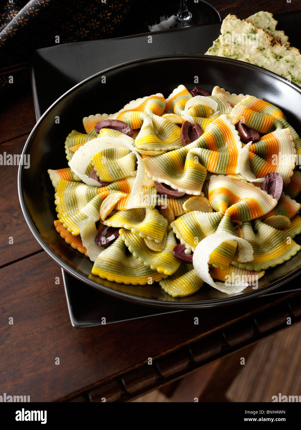 three color bow tie pasta in black bowl with garlic olives and Parmesan ...