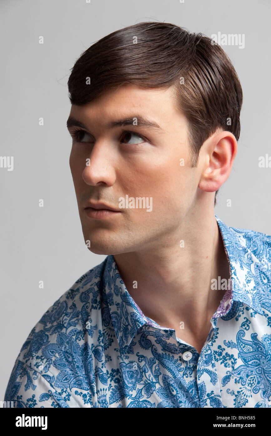 Young man wearing a blue shirt shot against a plain background looking ...