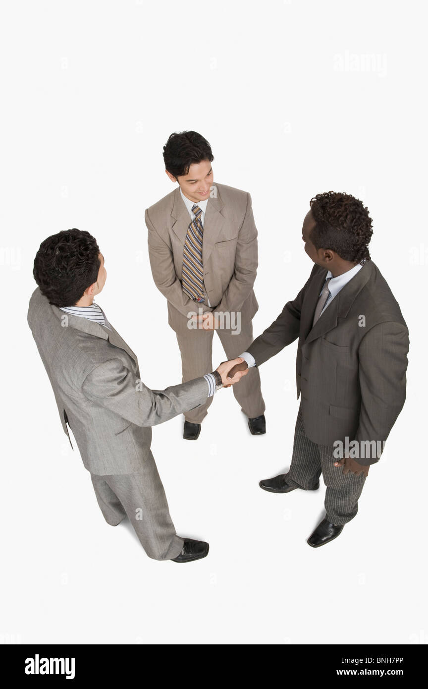 Two businessmen shaking hands with another businessman standing beside ...