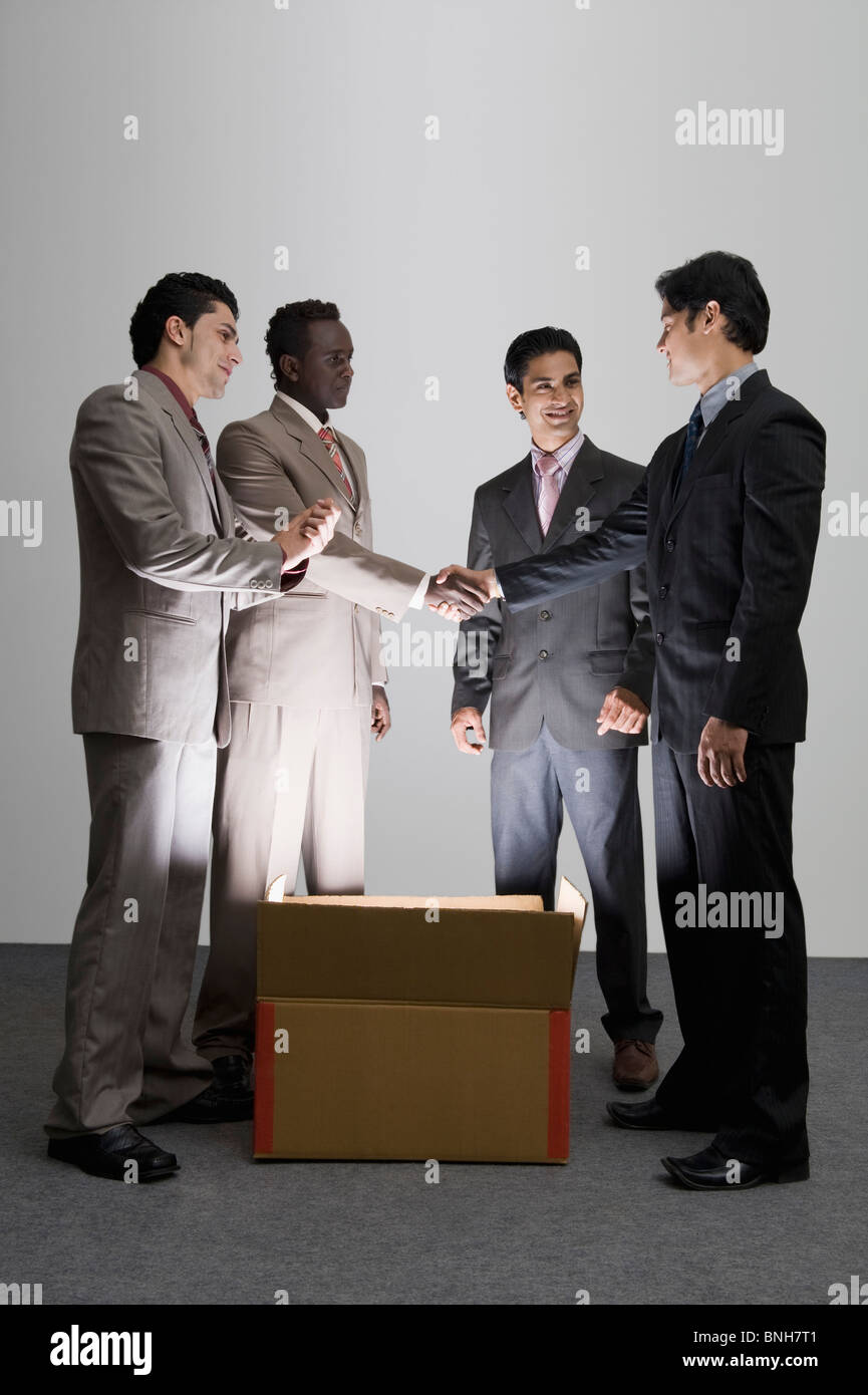 Two businessmen shaking hands over an illuminated cardboard box with ...