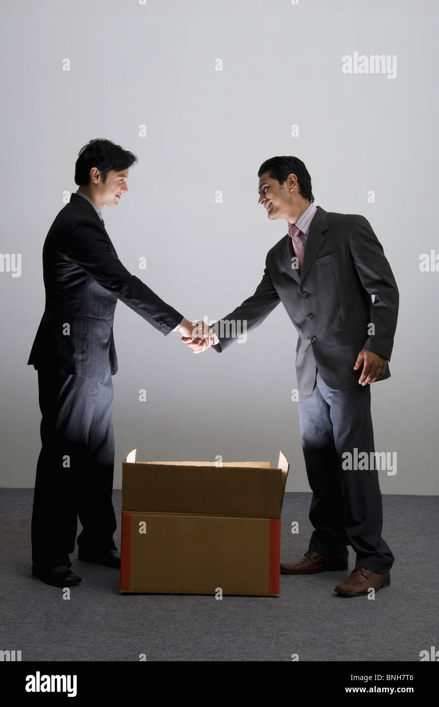 Two businessmen shaking hands over an illuminated cardboard box Stock ...
