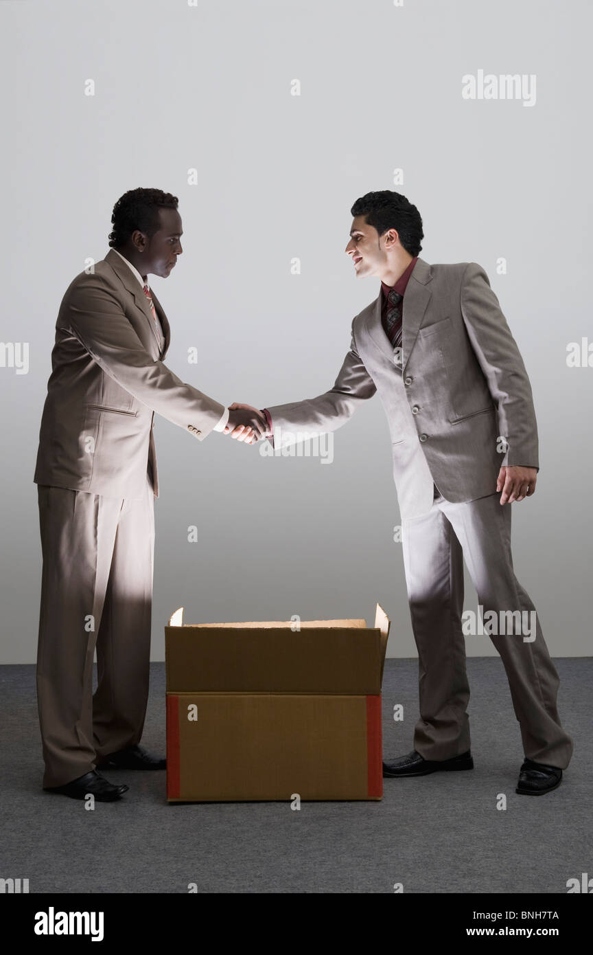 Two businessmen shaking hands over an illuminated cardboard box Stock ...