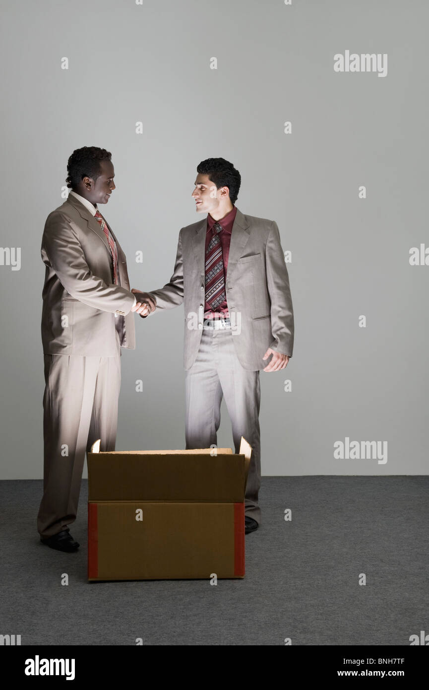 Two businessmen shaking hands over an illuminated cardboard box Stock ...
