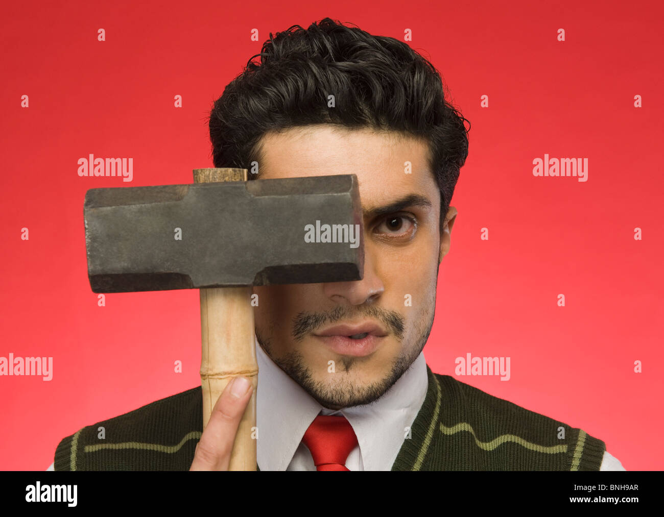 Portrait of a businessman holding a sledgehammer in front of his face ...