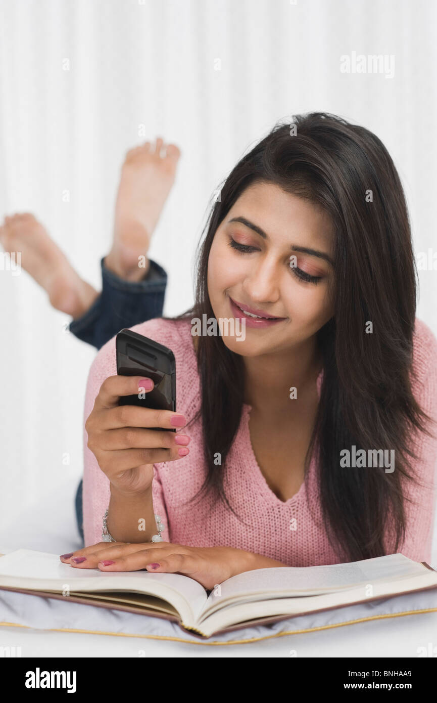 Woman using a mobile phone while reading a book Stock Photo - Alamy