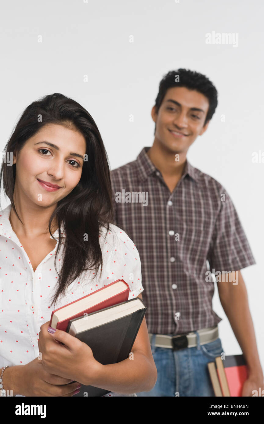 Portrait of a woman holding books with her friend in the background ...