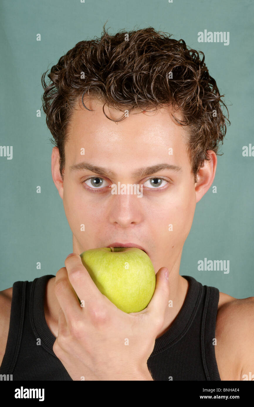 Young man biting a granny smith apple over a green background. Concept ...