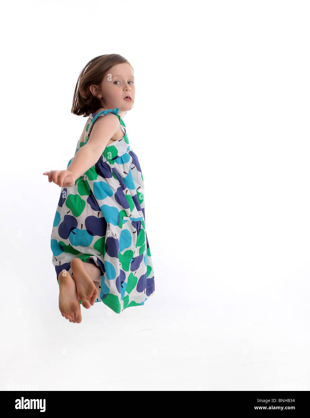 Young female child jumping in studio environment looking back over her ...