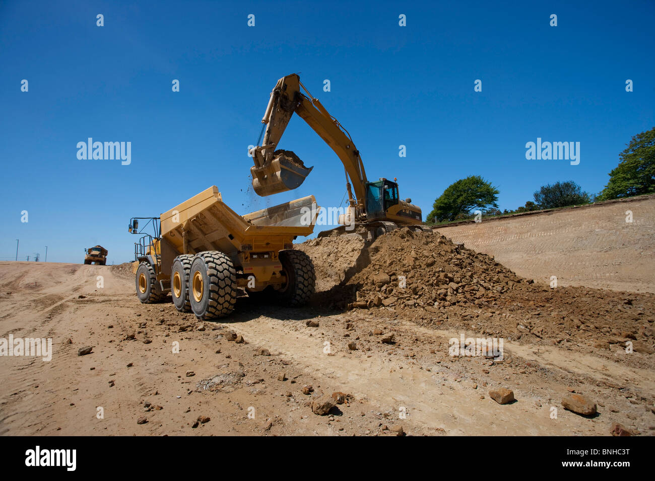 Articulated earth mover and excavator on road construction site Stock ...