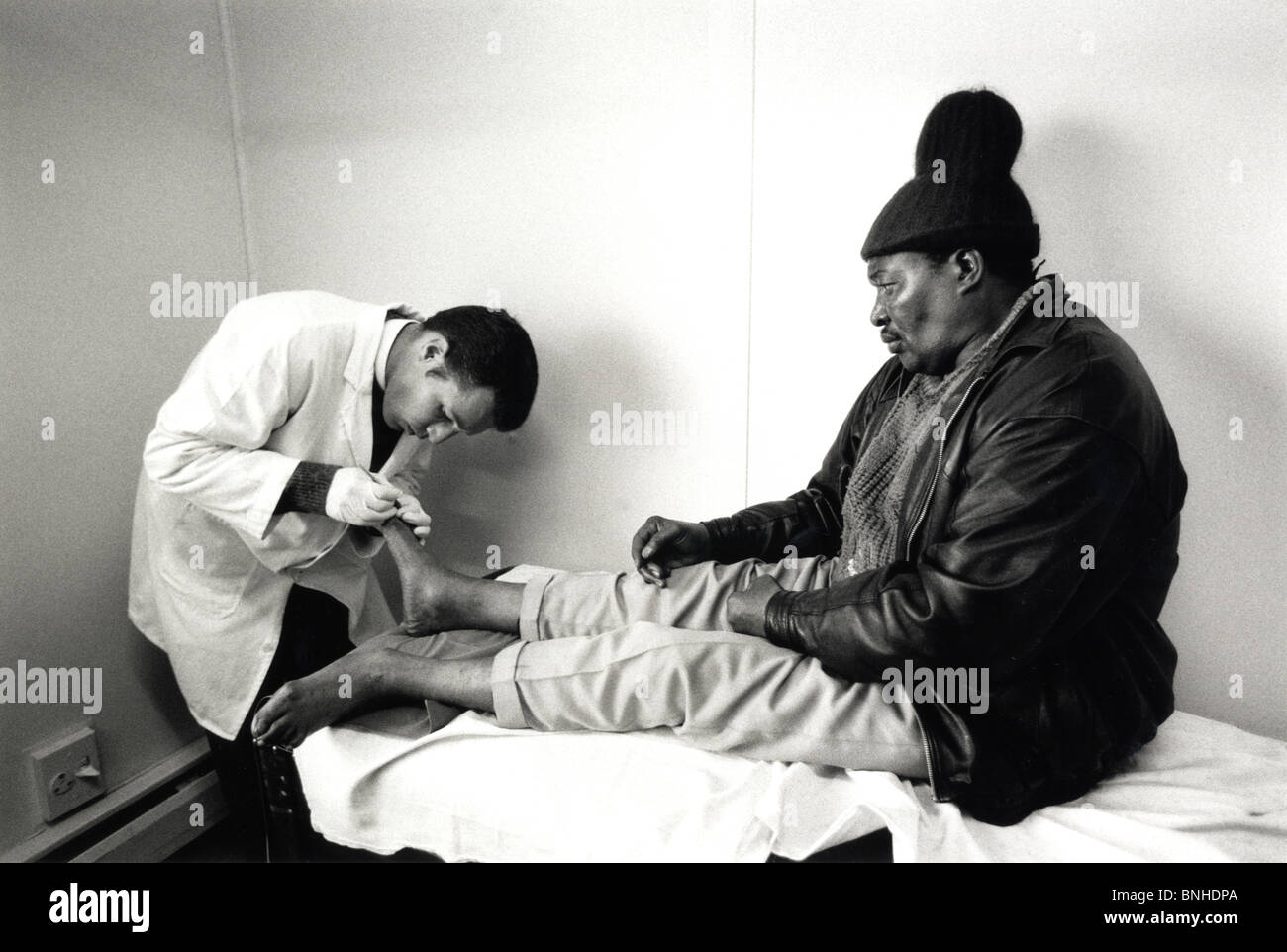 Young male white doctor examines the feet of an elderly black male ...