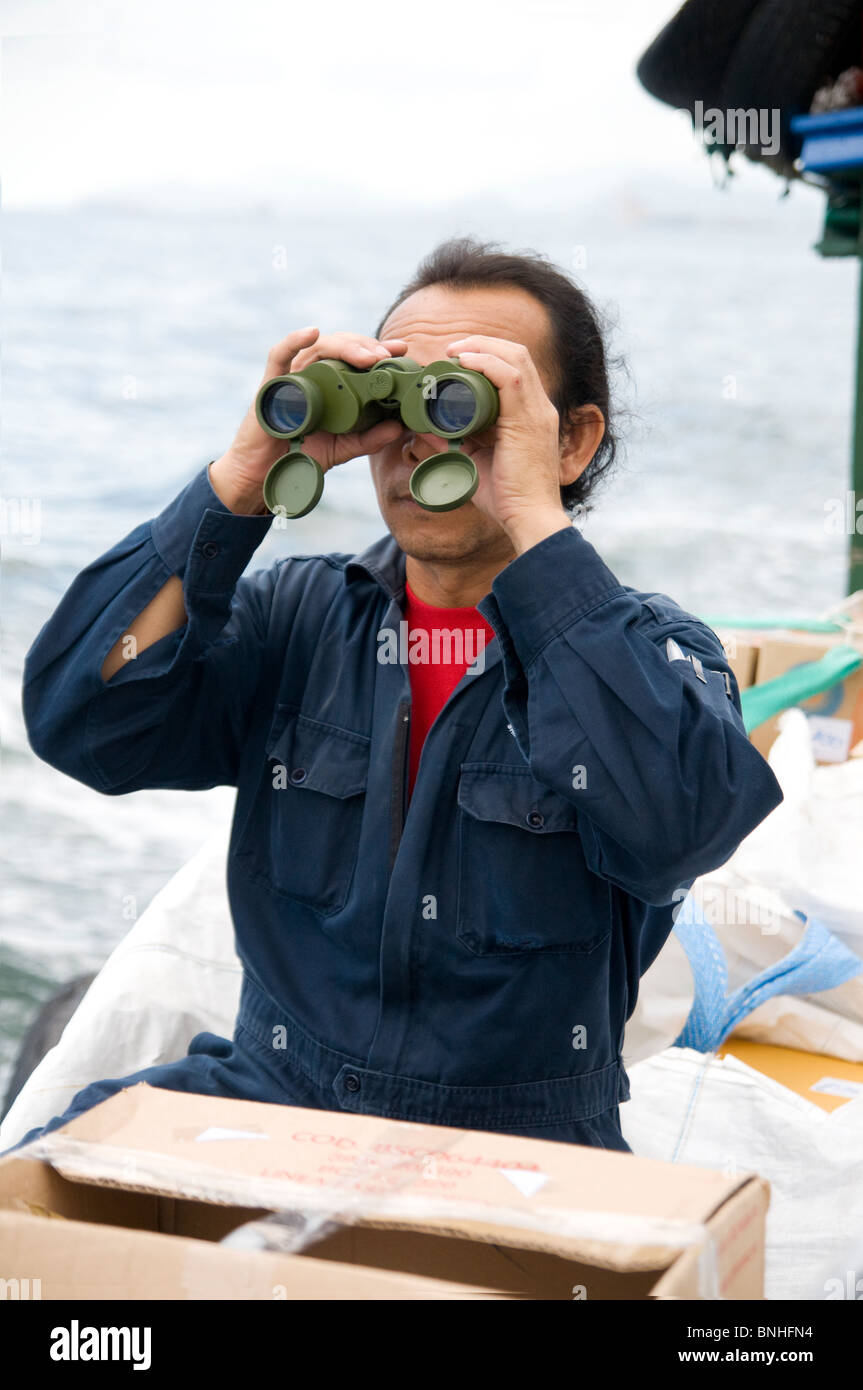 Sailor dressed in blue coverall on a small vessel looking through ...