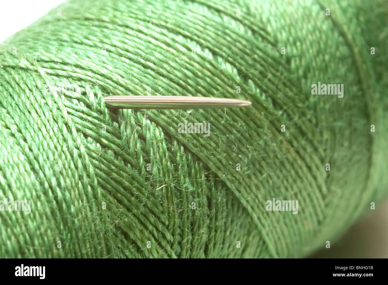 Green sewing thread and a needle sharp Stock Photo - Alamy