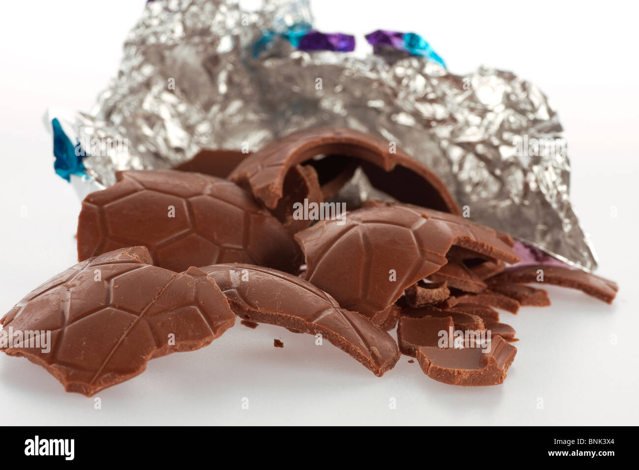 Broken pieces of milk chocolate Easter egg with silver & blue foil ...